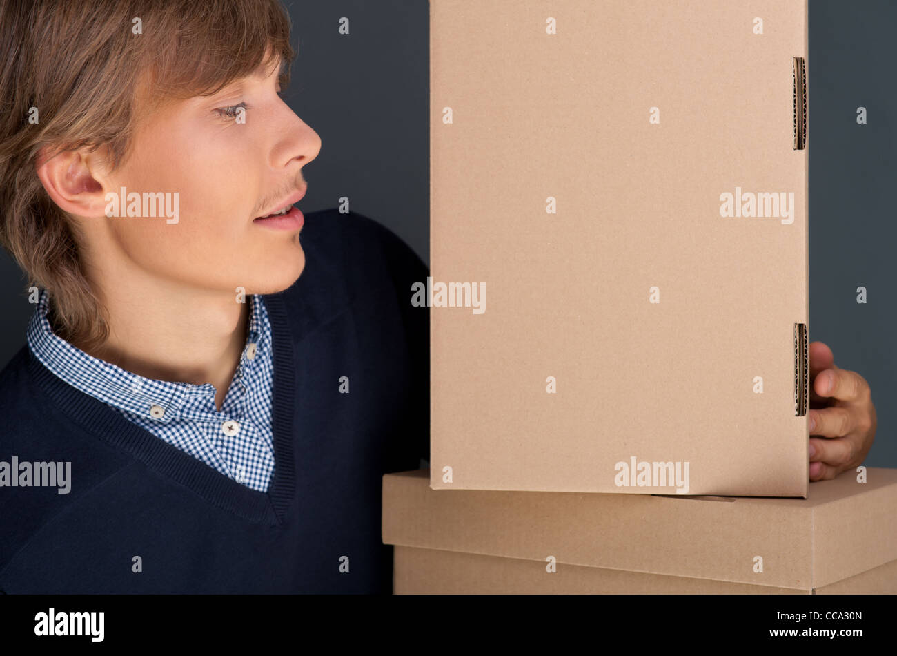 Portrait of young man leaning on box against grey wall. He is starting ...
