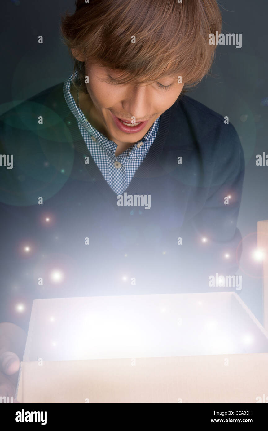 Portrait of young man opening gift box. He is happy. Magical shine ...