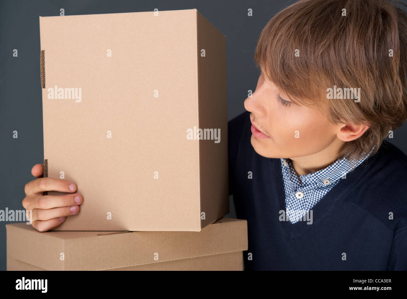 Portrait of young man holding on box against grey wall. He is starting ...