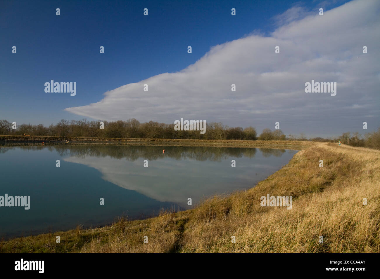 The sharp edge of a cloud bank is reflected in the perfectly still blue ...