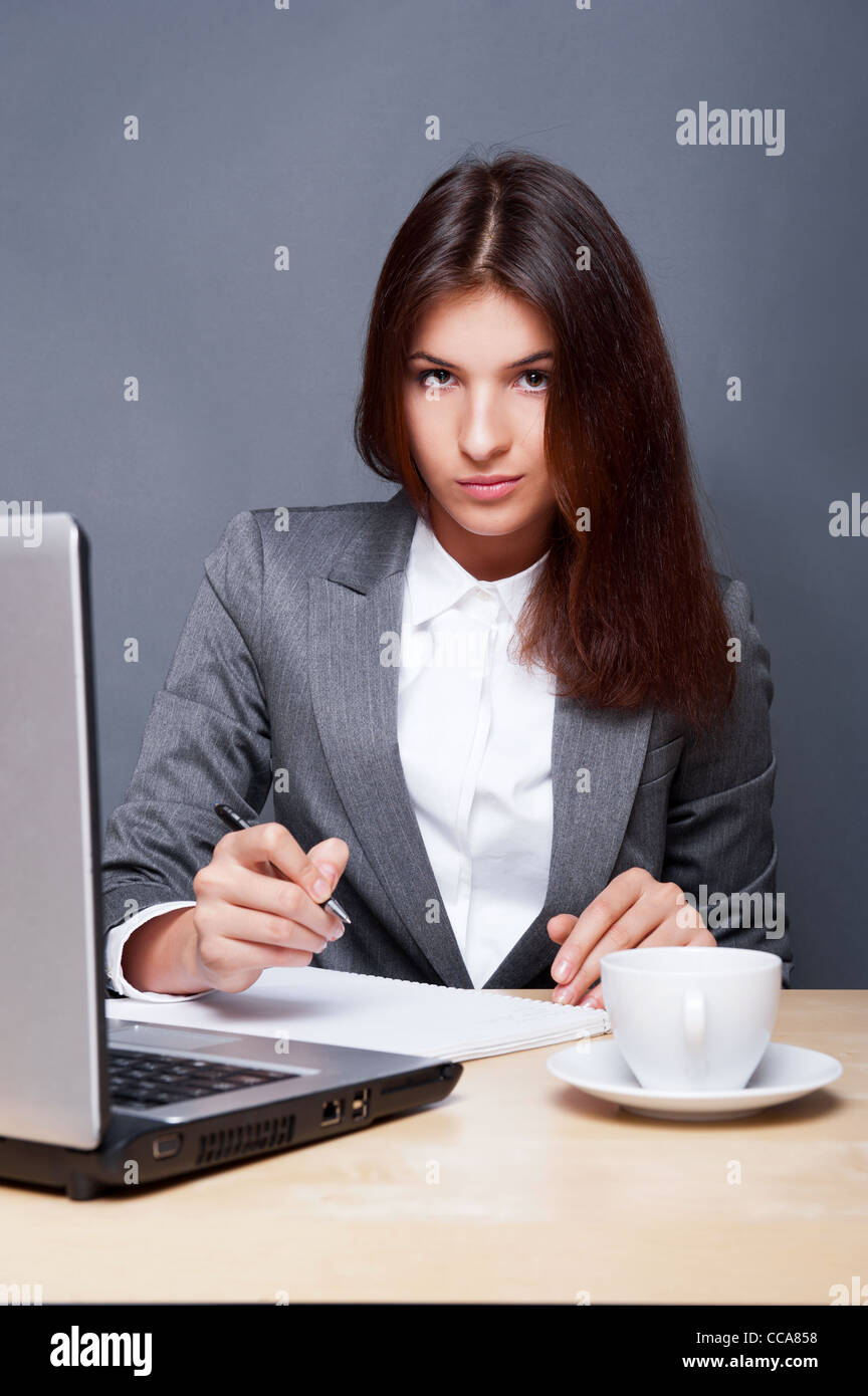 A pretty concentrated woman working with her laptop and papers. Sitting ...