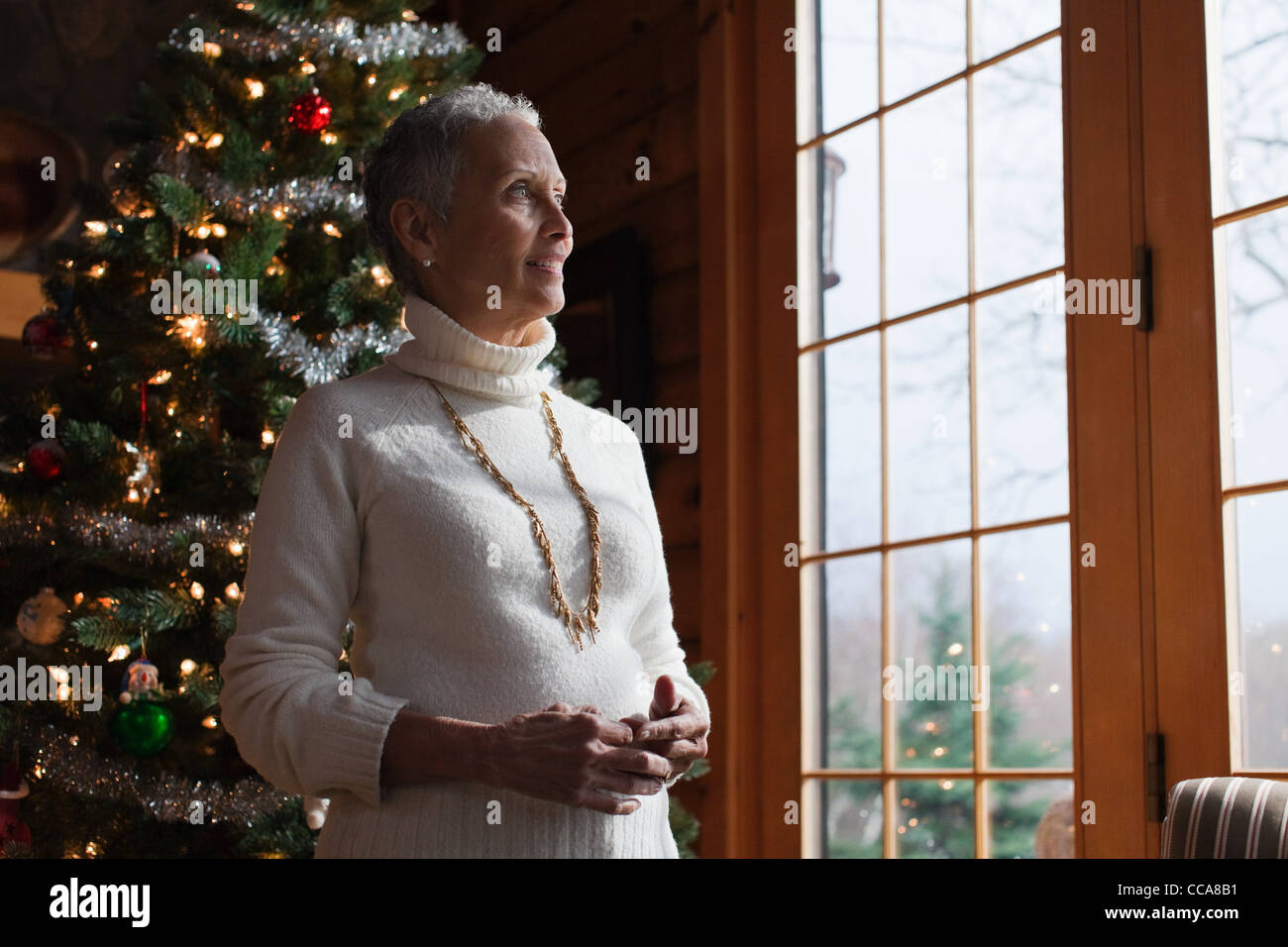 Mature woman standing by Christmas tree, looking through window Stock ...