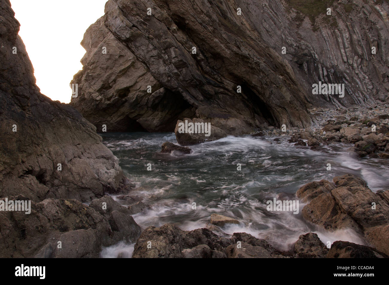 Waves surge through a rocky inlet into Stair Hole. The tilted rock ...