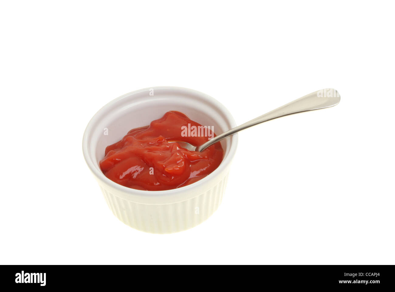 Tomato ketchup with a spoon in a ramekin isolated against white Stock ...