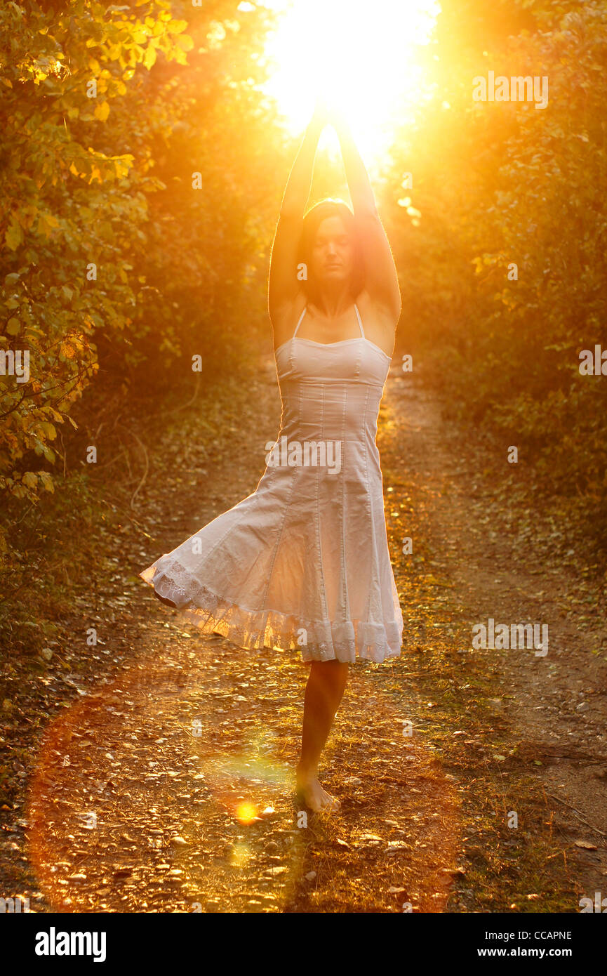 Beautiful young woman balancing on one leg meditating with hands above ...