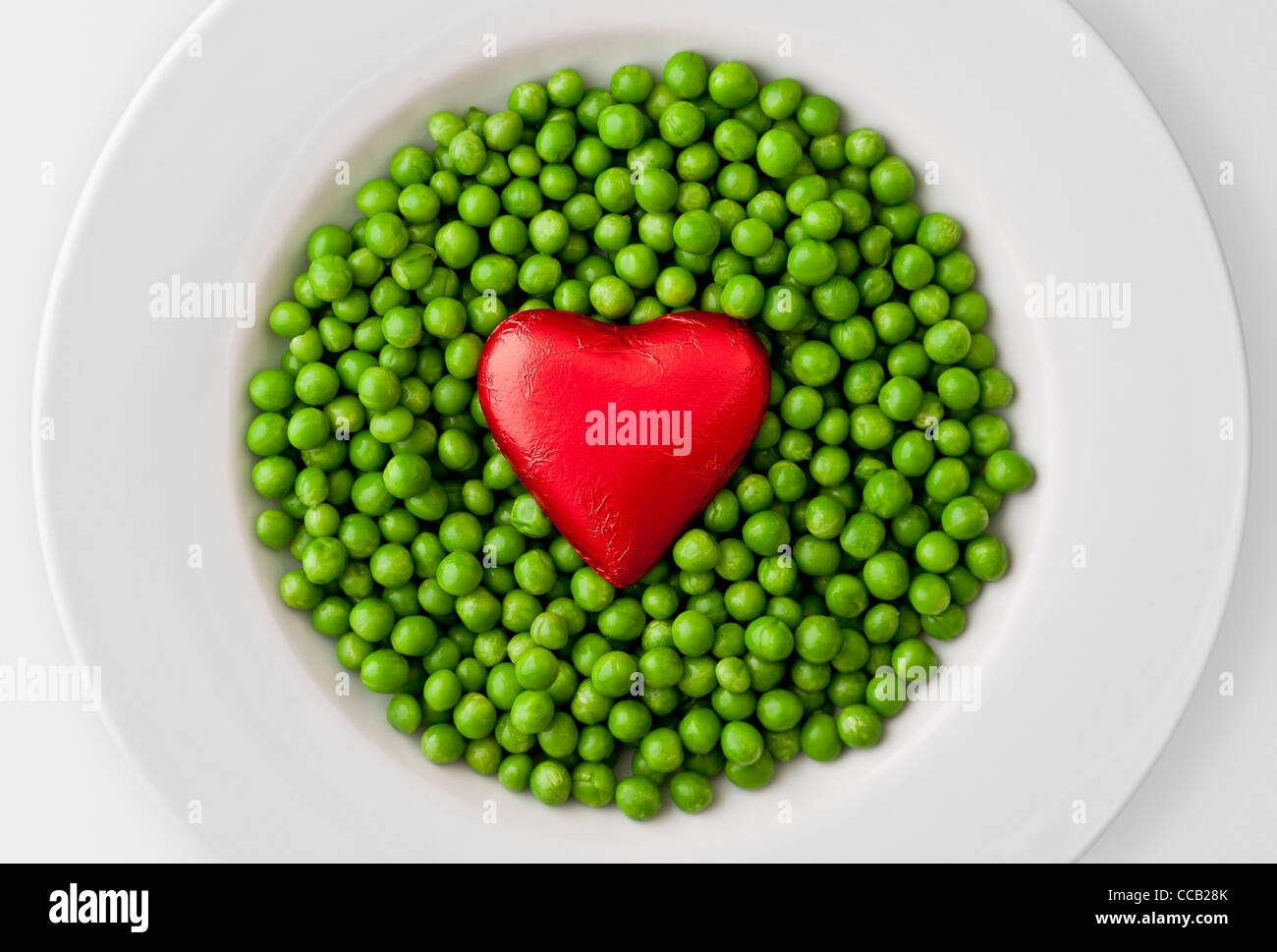 Red heart on fresh green peas. White plate, white background Stock ...