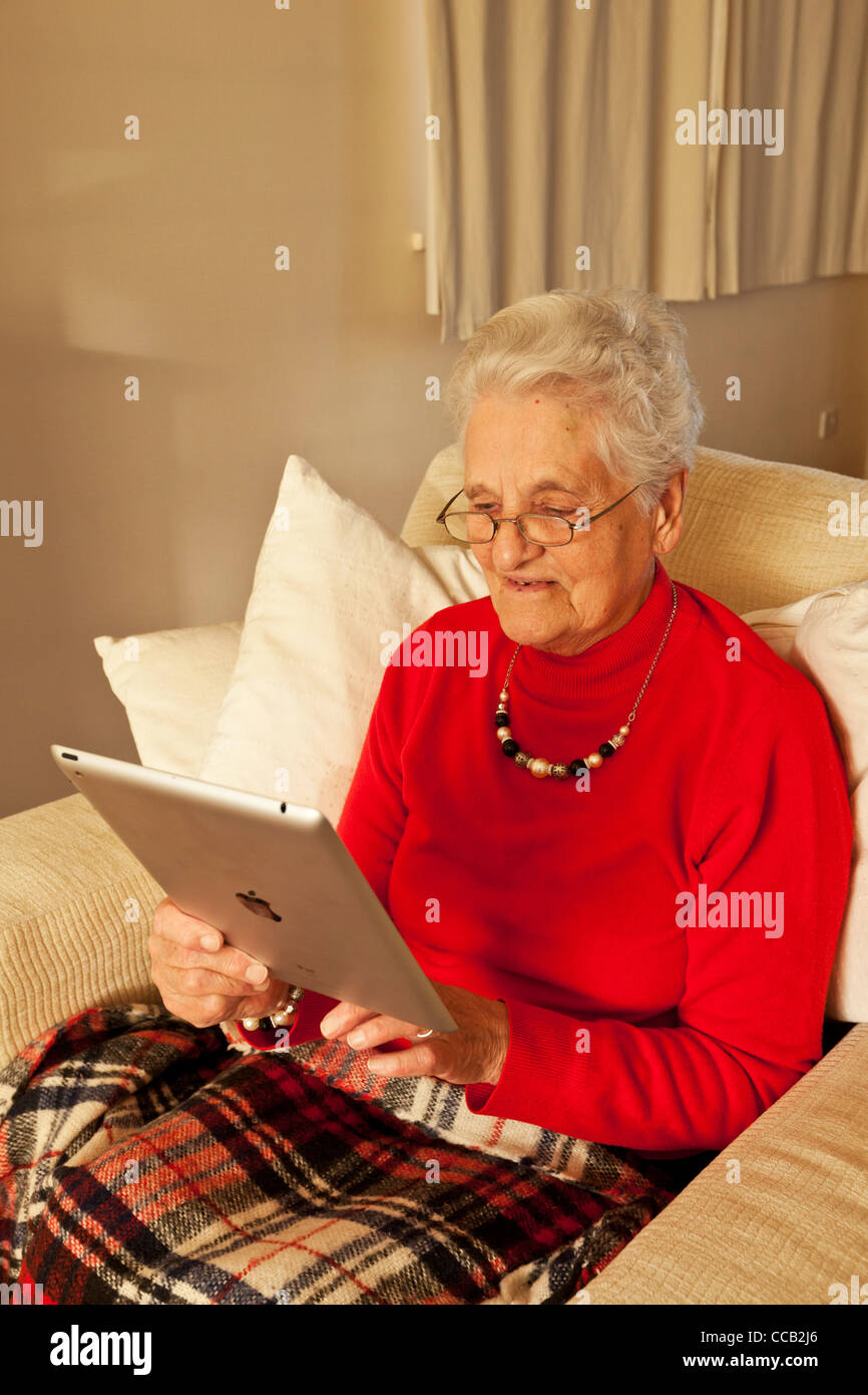 Old Woman using an Ipad 2 computer tablet sat in an armchair wearing ...
