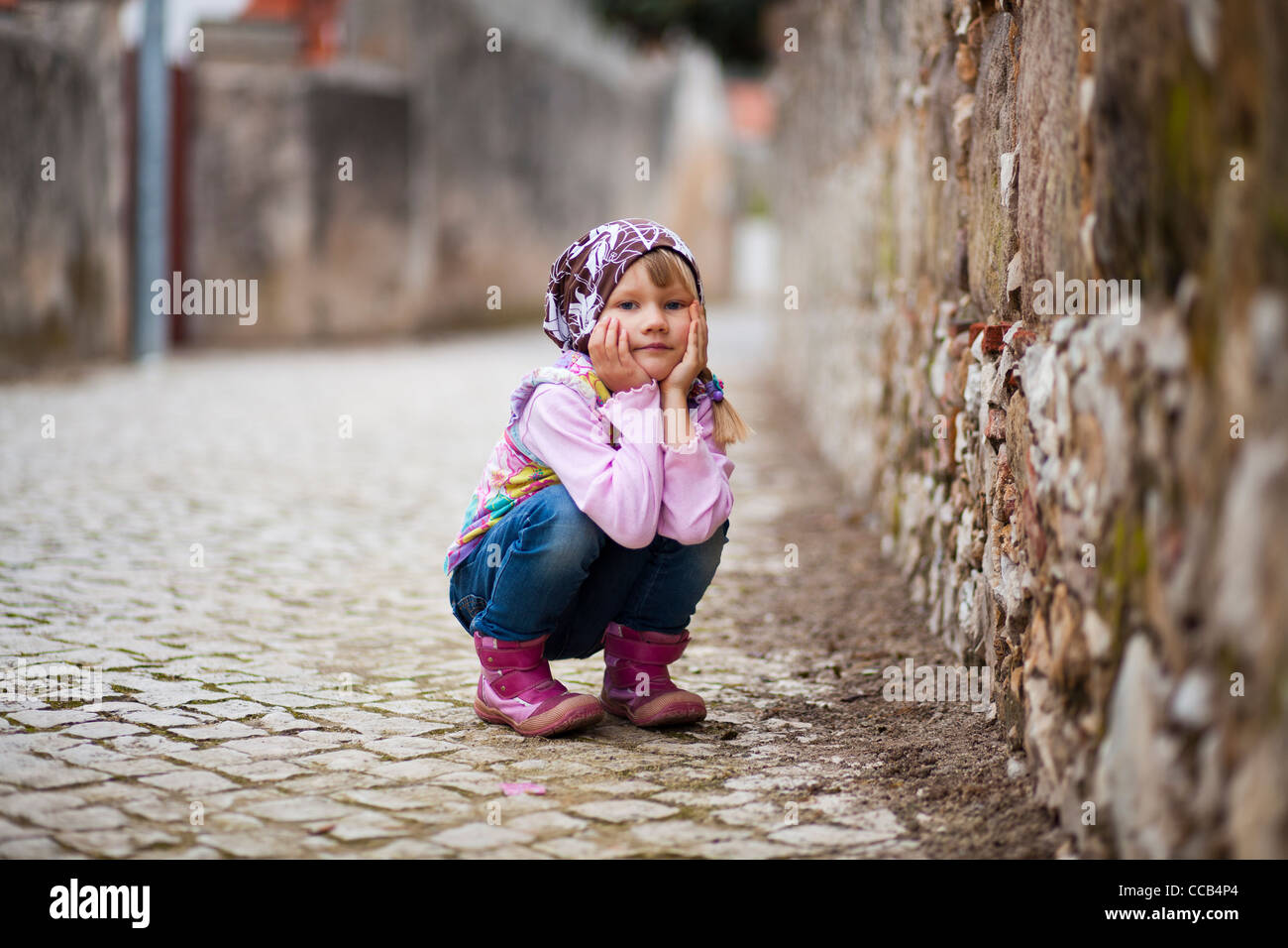 Portrait of a little girl outdoors on a city street, hands on cheeks ...