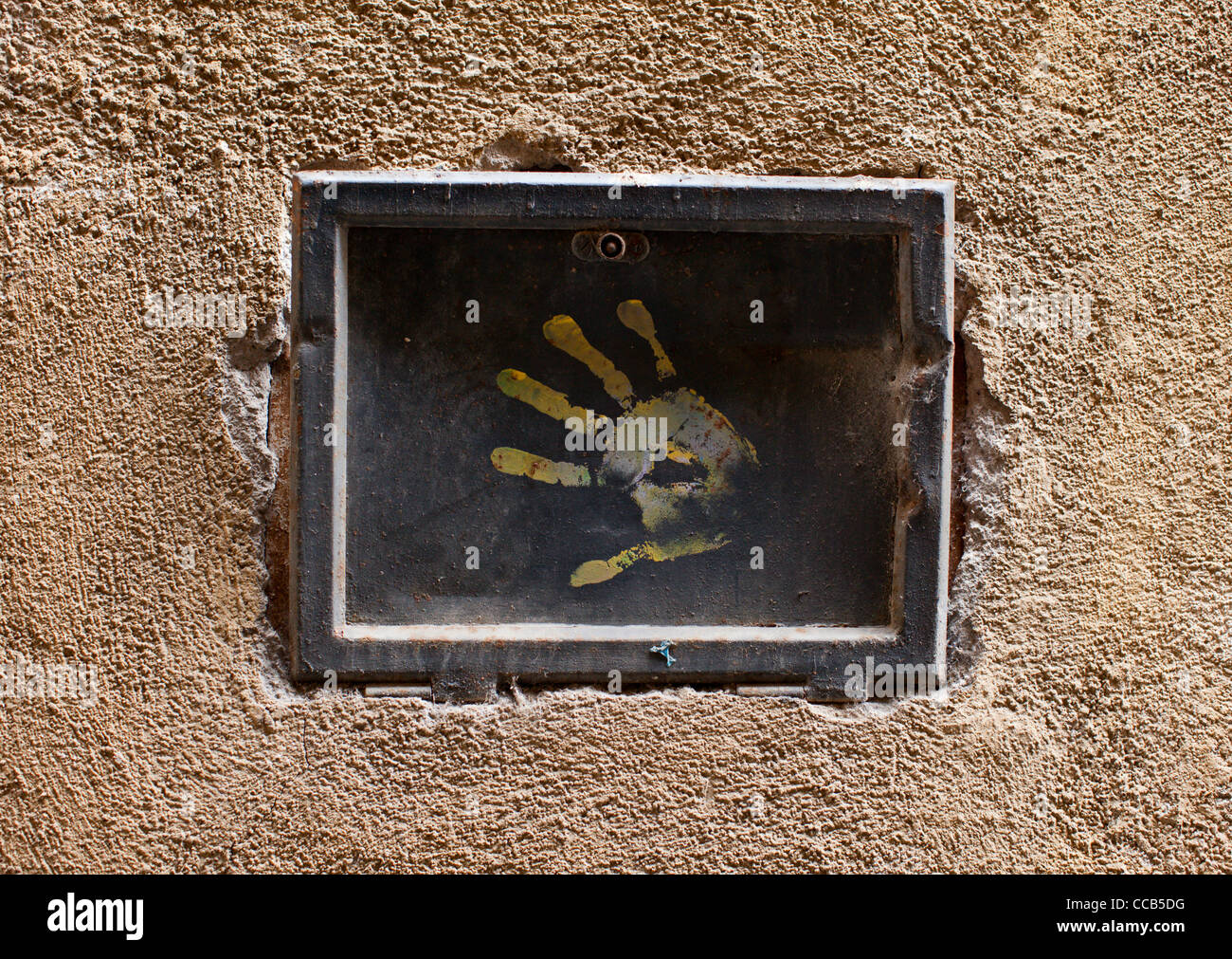 An electricity fuse box sunken into a plaster wall with a hand print on ...