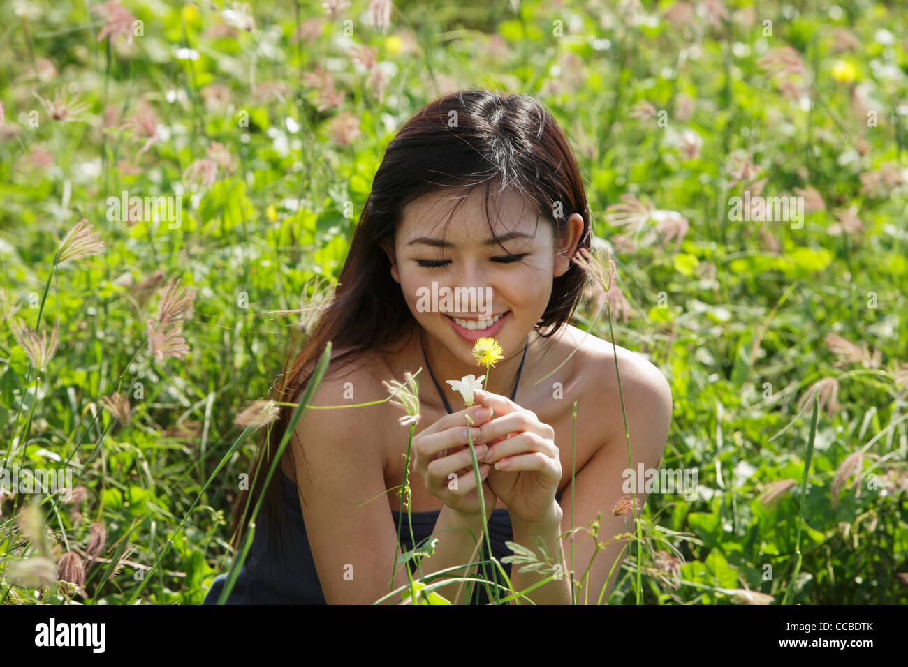 young woman looking at flower in grassy field Stock Photo - Alamy