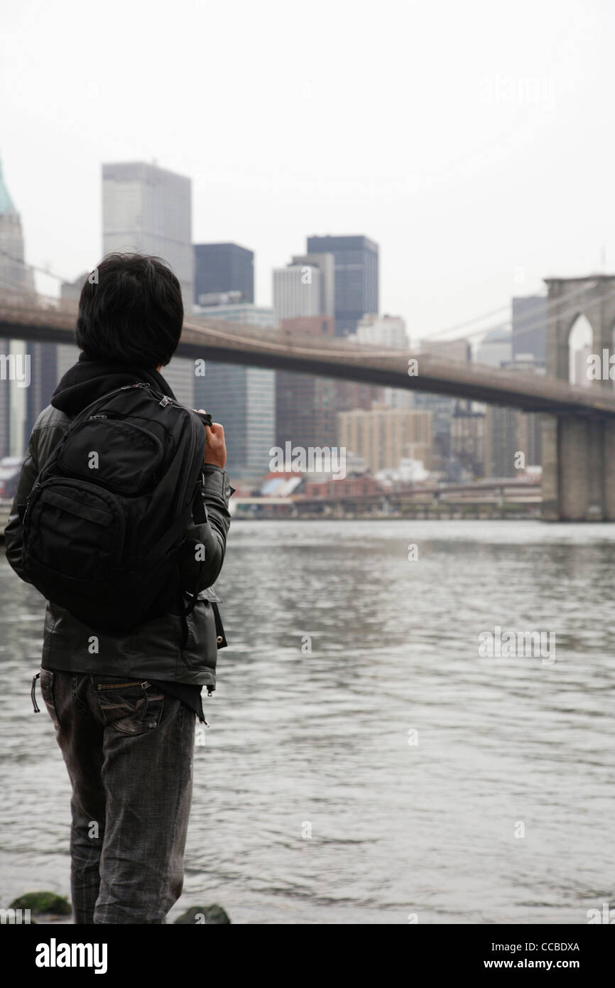young man wearing a back pack while looking at the city skyline and ...