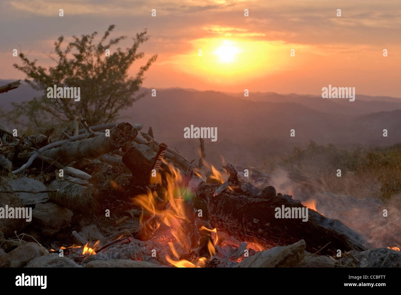 Landscape of a campfire at sunset with the sun setting over the distant ...