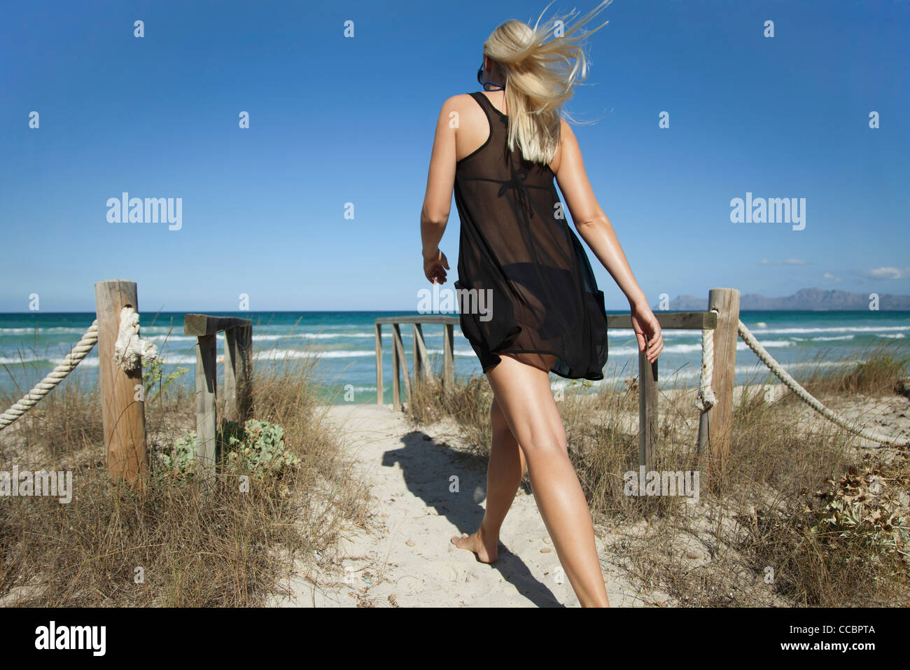 Woman walking on beach path toward sea, rear view Stock Photo - Alamy