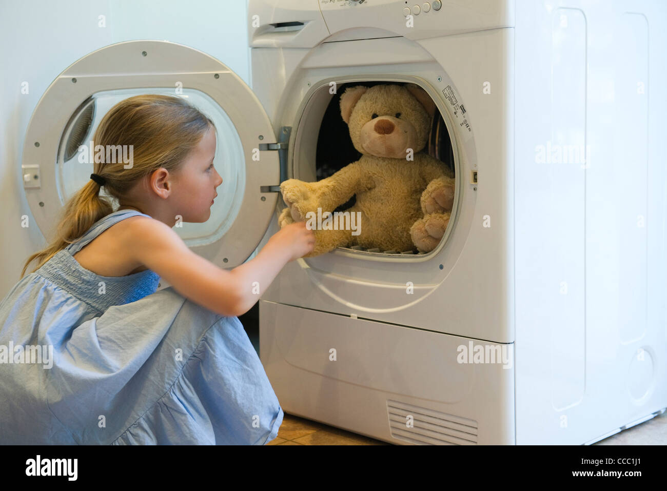 Little girl taking teddy bear out of dryer Stock Photo - Alamy