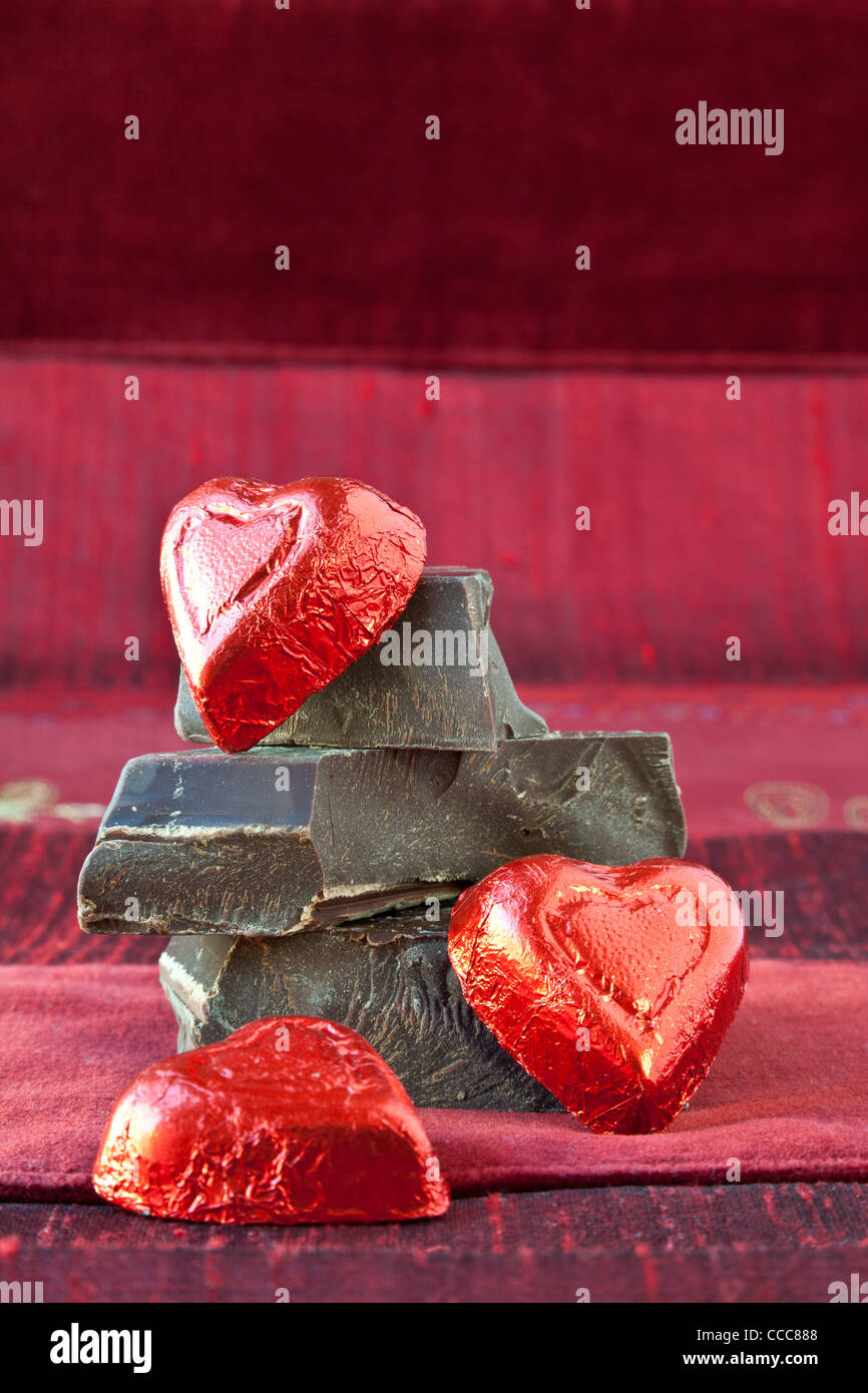 Red foil wrapped candy hearts arranged on top of pile of gourmet thick ...
