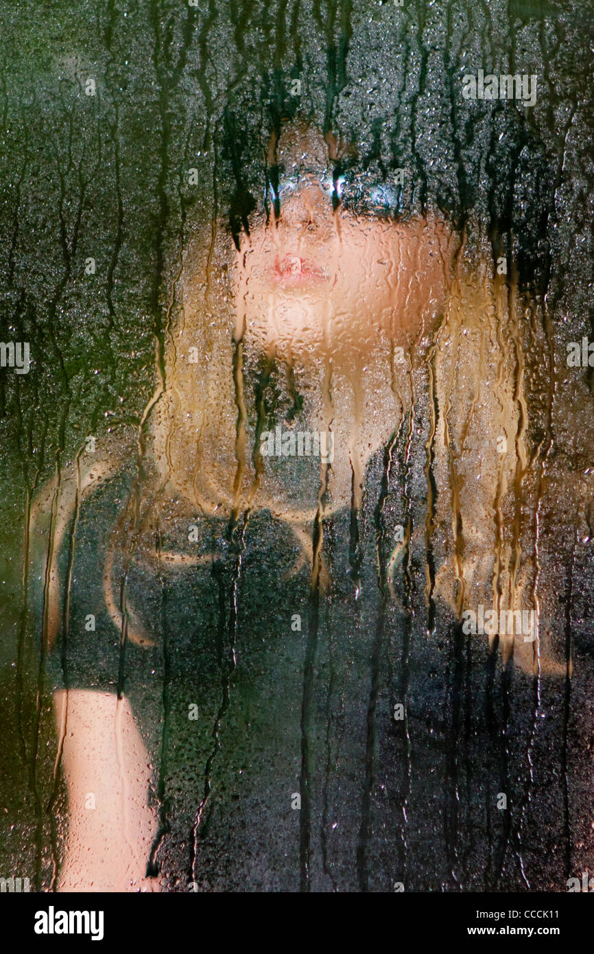 Young girl wearing sunglasses and looking into the rain through a ...