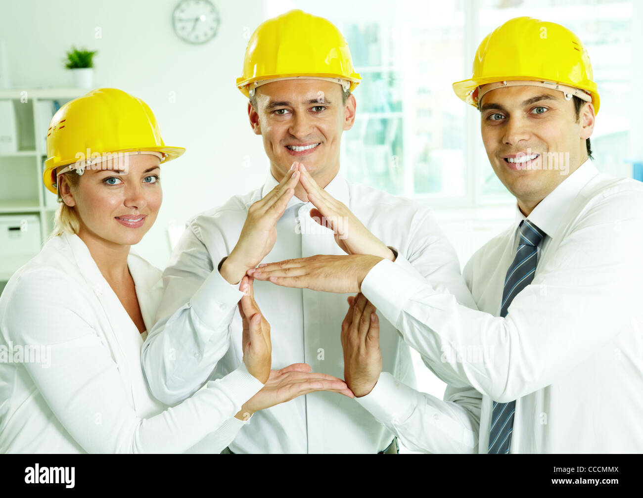 A group of smiling architects in helmets showing hand sign of house ...