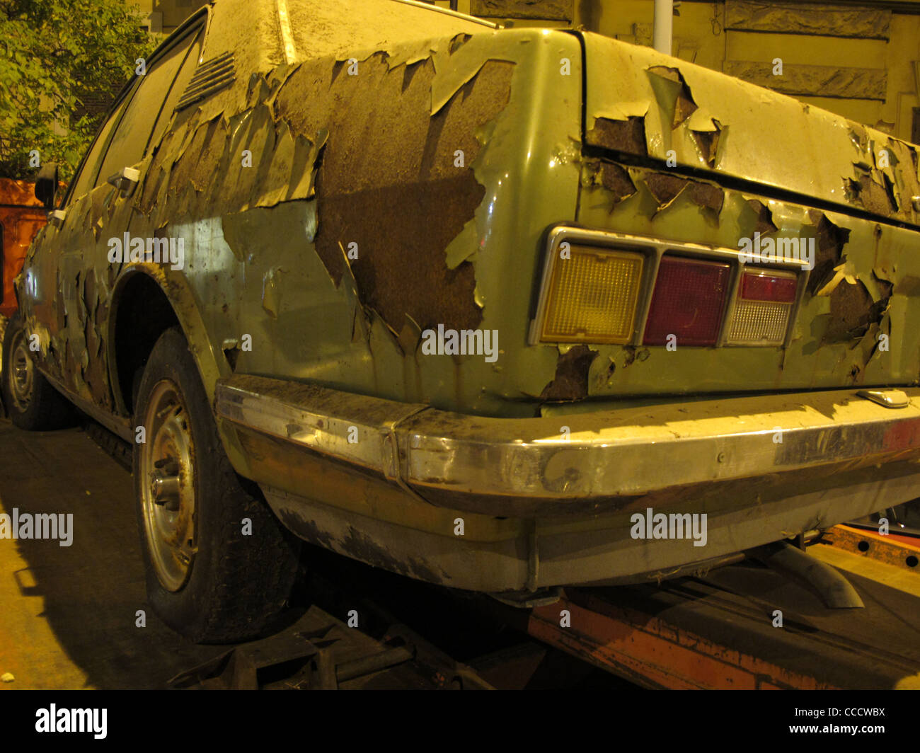 abandoned old damaged car on tow away truck lorry at night in city town ...