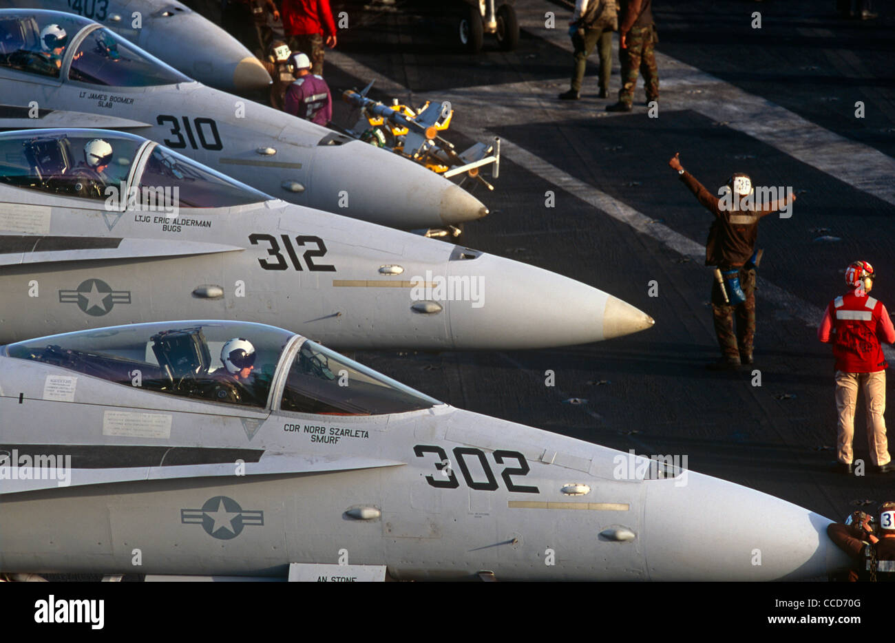Red shirted ordnance men organise the busy deck of F/A-18C fighter jets ...
