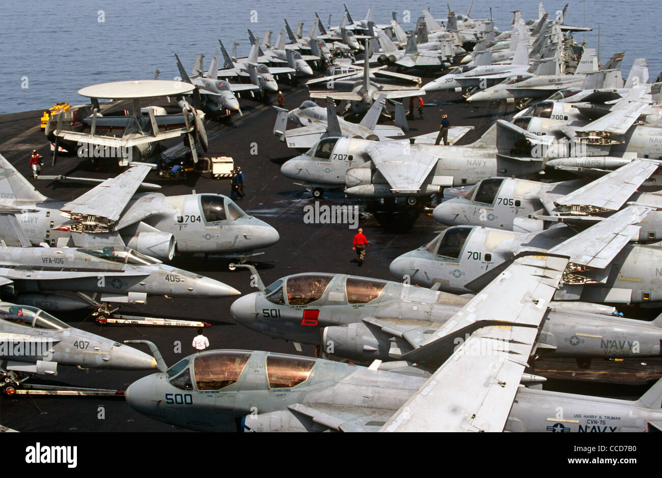 A red shirted ordnance man walks through a crowd of US Navy fighter and ...