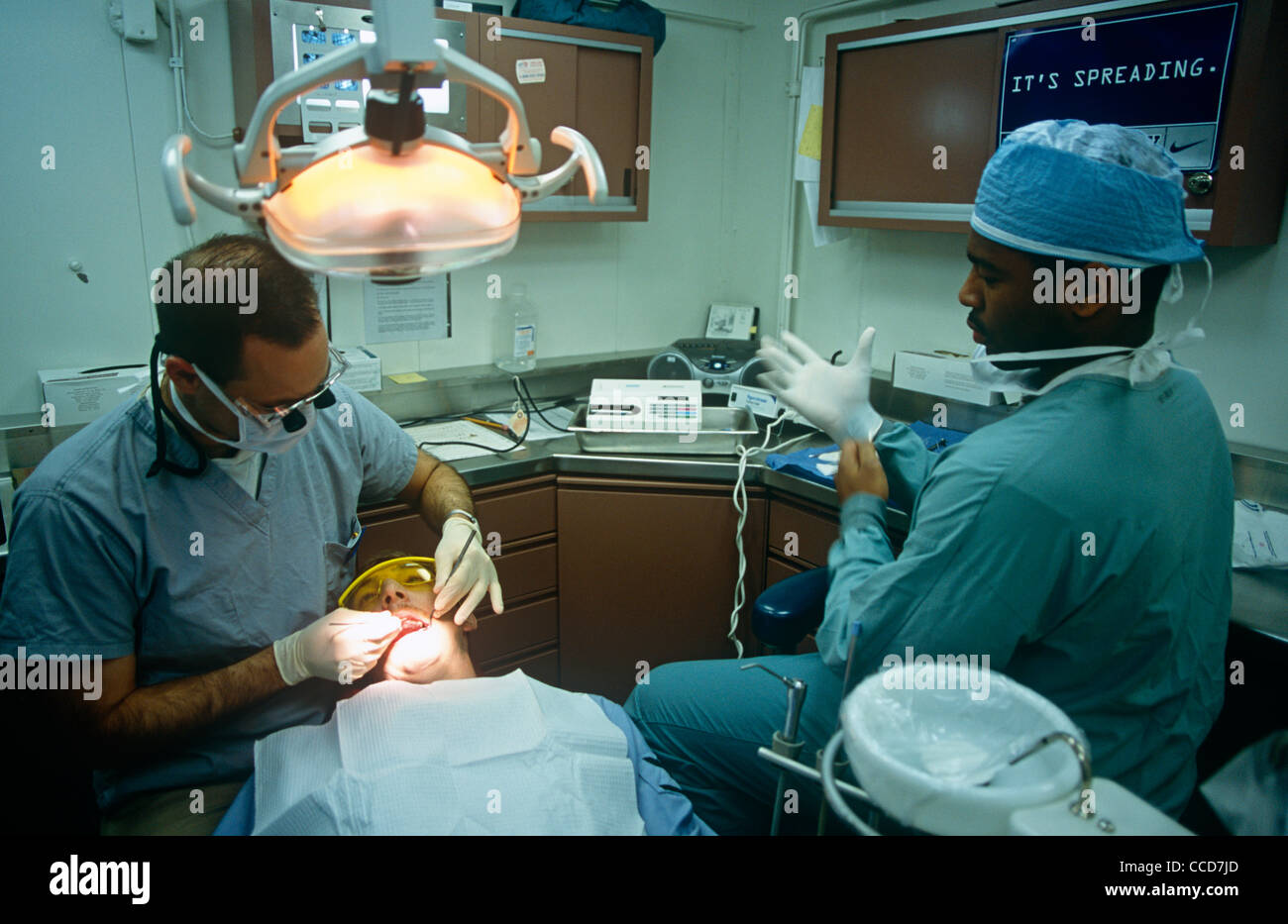 A US Navy dentist and technician inspects the mouth of a sailor below ...