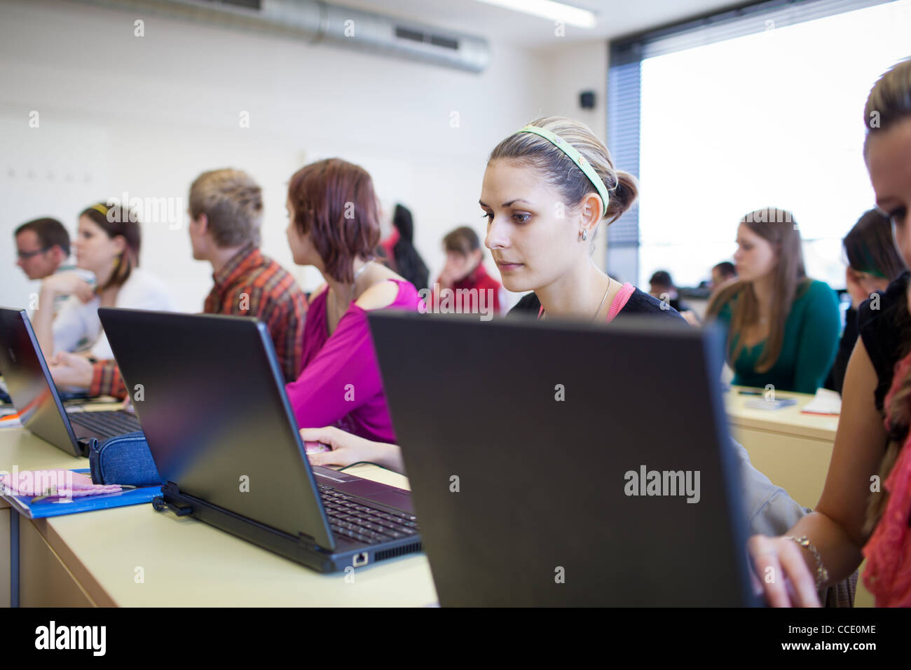 college students sitting in a classroom, using laptop computers during ...