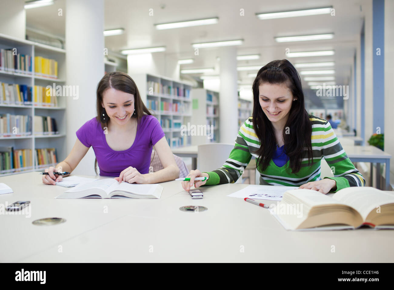 in the library - two female students with books working in a high ...