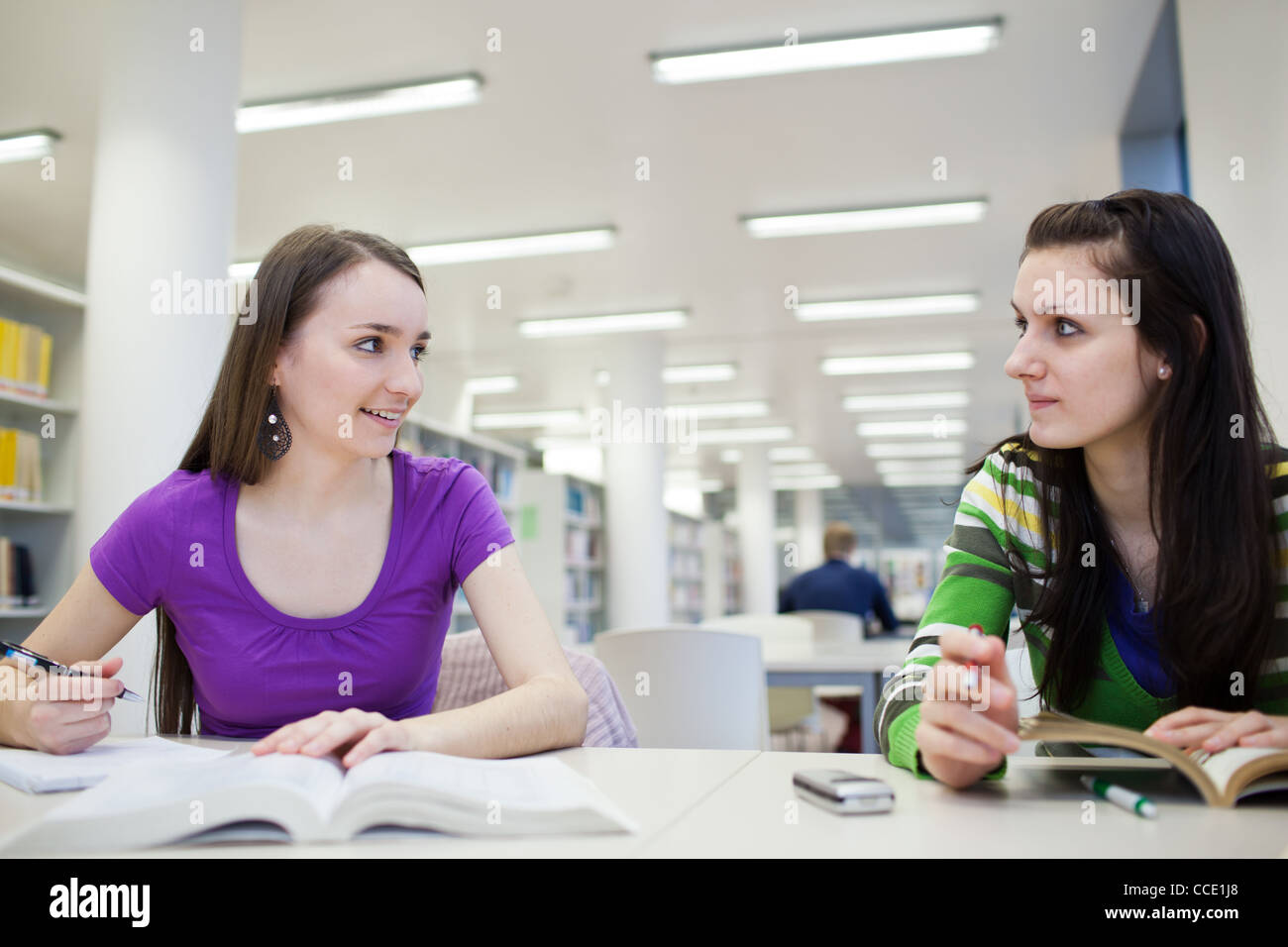 in the library - two female students with books working in a high ...
