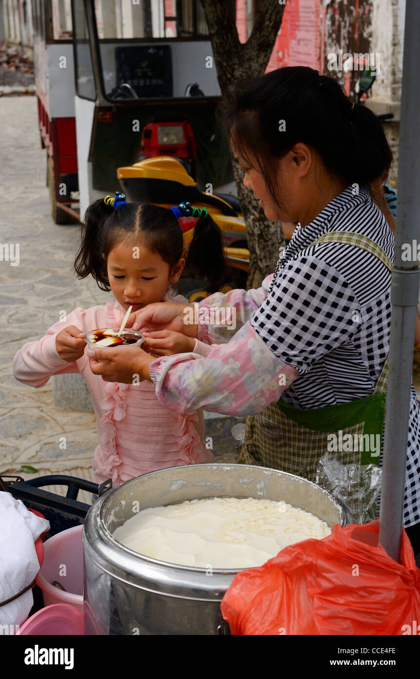 Street vendor giving fresh curd Douhua to a young school girl in Fuli ...