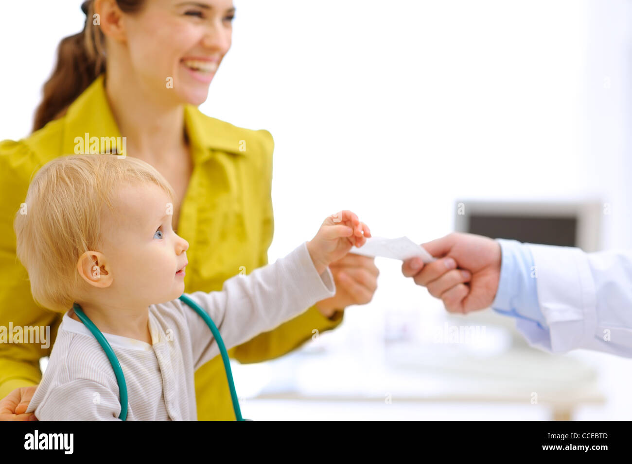 Mother and baby stretching for prescription in hand of pediatric doctor ...