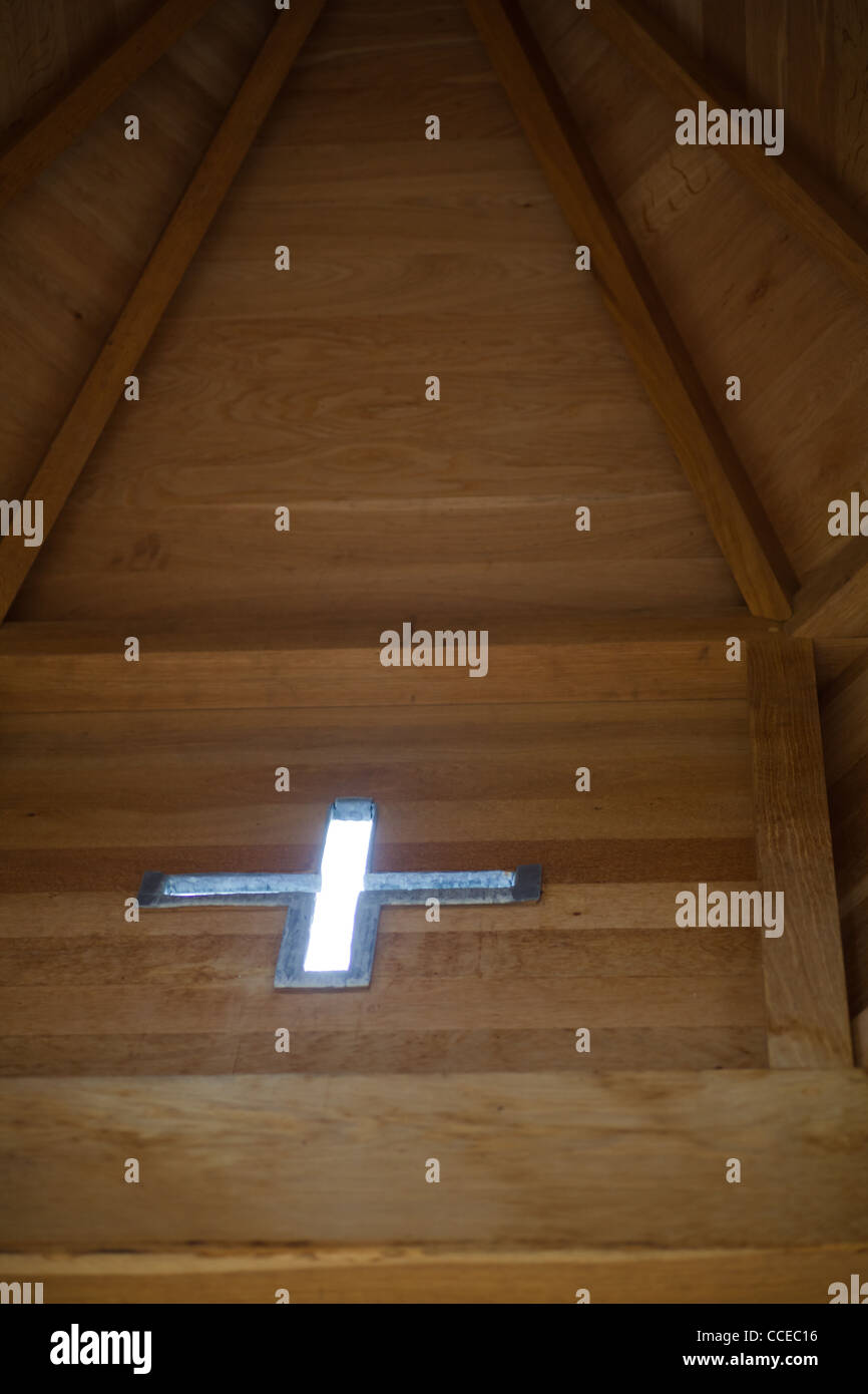 Looking up at a wooden roof of a small chapel. A cross shaped window ...