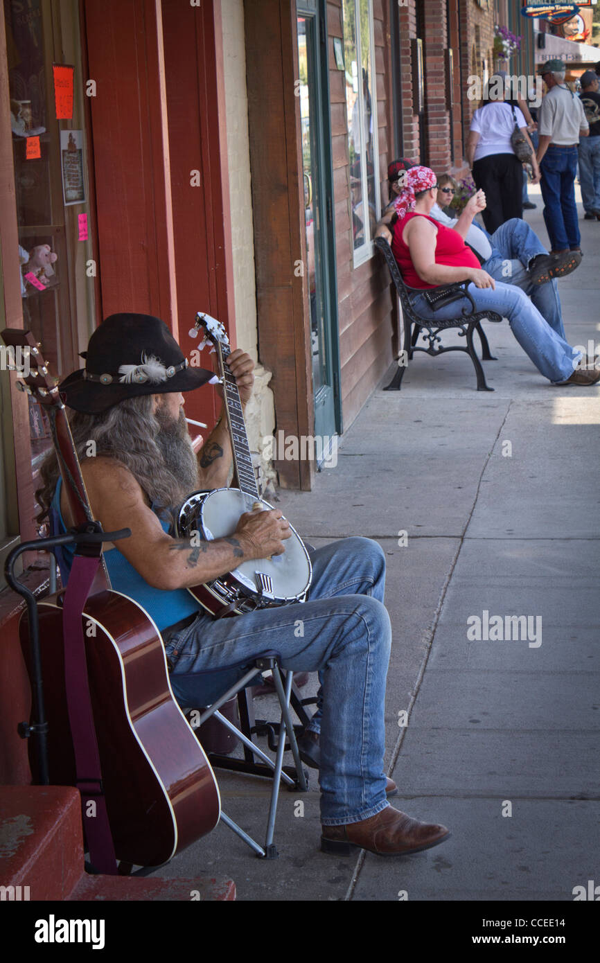 A man plays on a bango on a city street USA View of a small town street ...