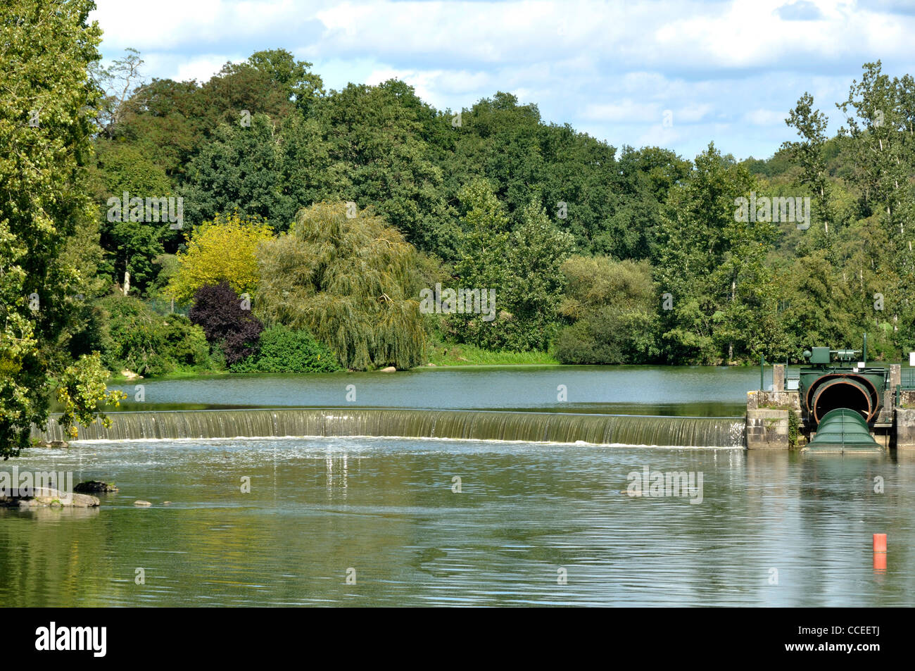 A dam on a river with hydro electric turbine, Mayenne river, towpath of ...