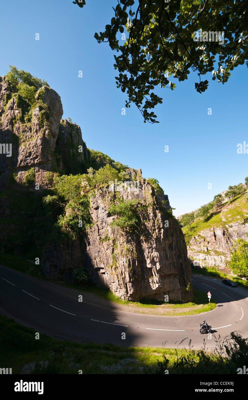 A motorcyclist riding around a bend in the road through cheddar Gorge ...