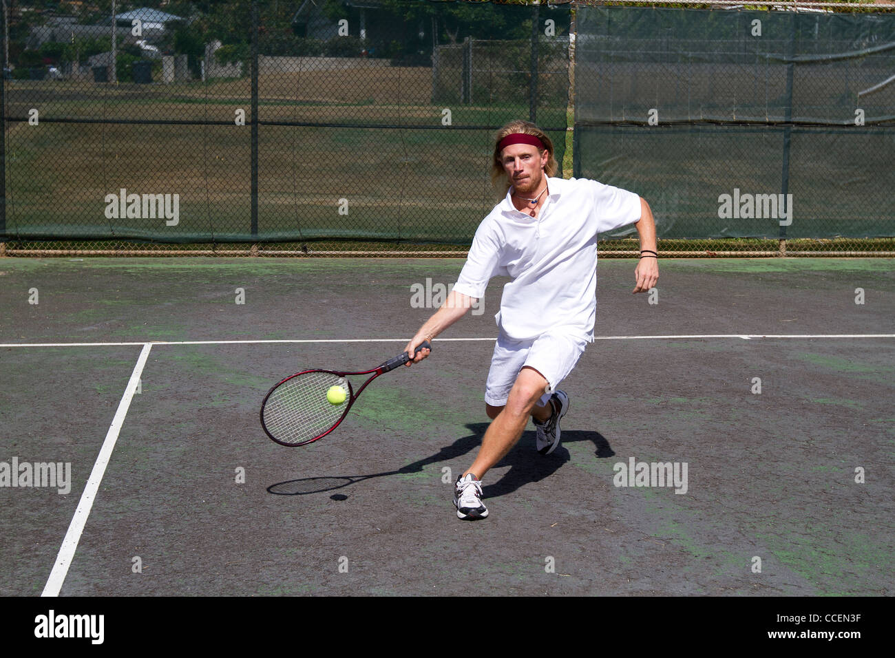 A blonde male tennis player takes a step into a solid forehand return ...