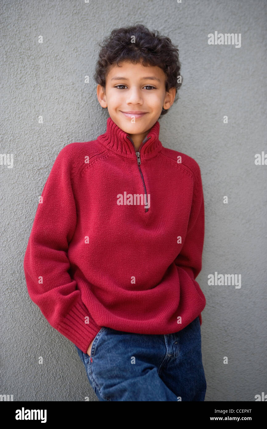 Happy mixed race person with hands in pockets standing against wall ...
