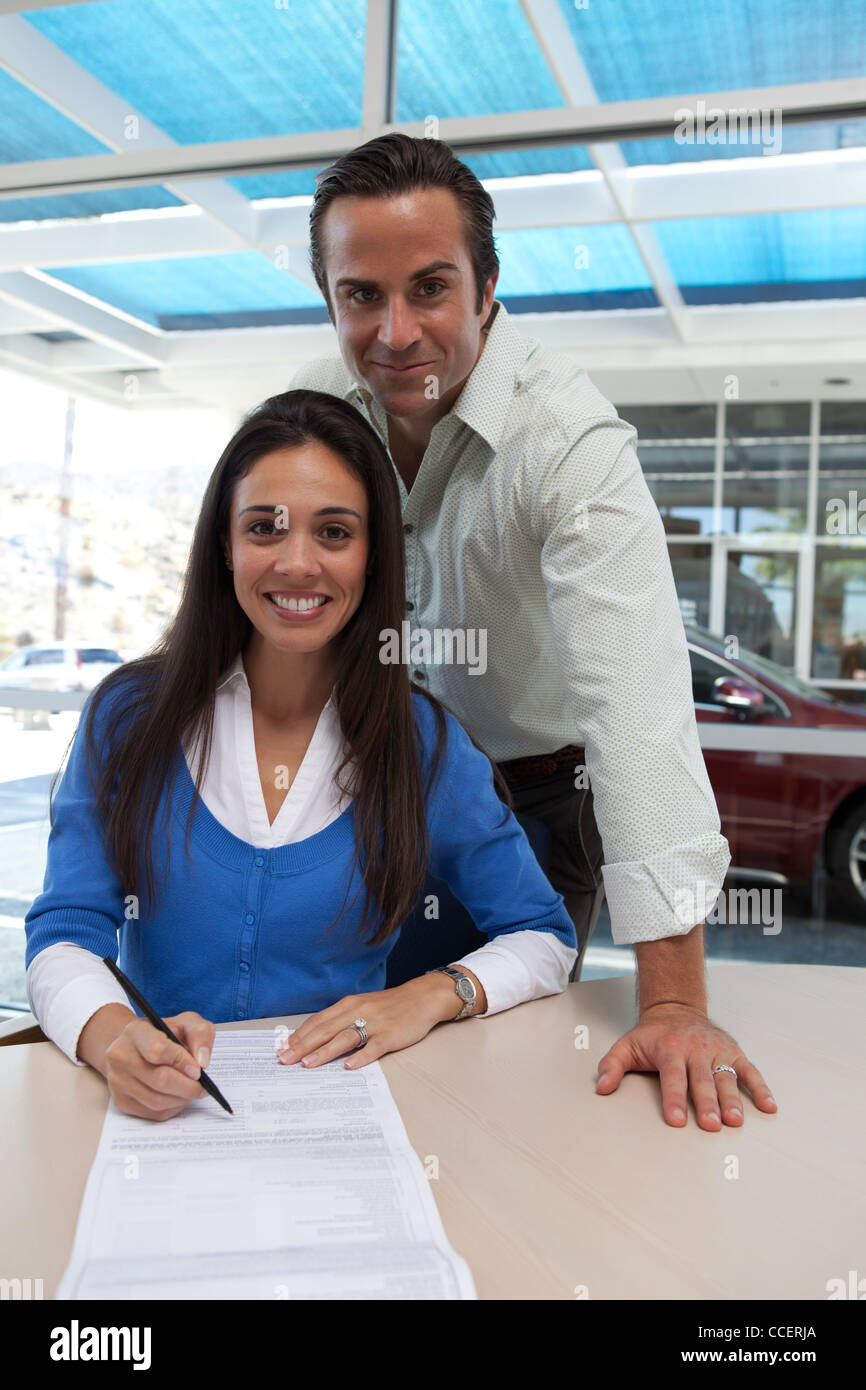 Portrait of woman signing car contract with husband standing behind ...