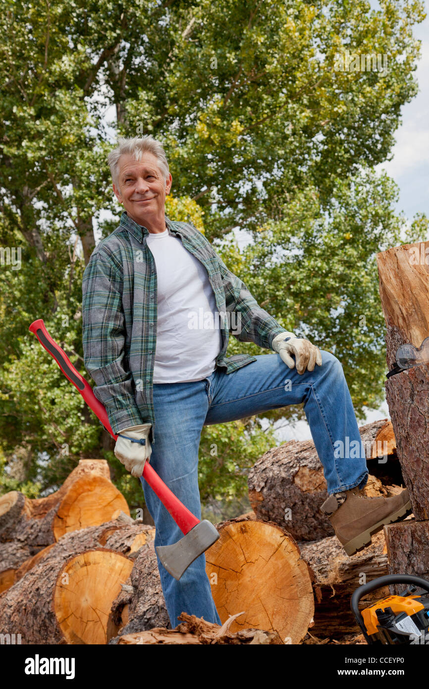 Lumberjack with an axe standing with stack of chopped firewood in ...