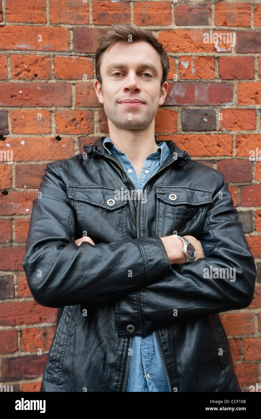 Portrait of man in leather jacket standing against brick wall Stock ...