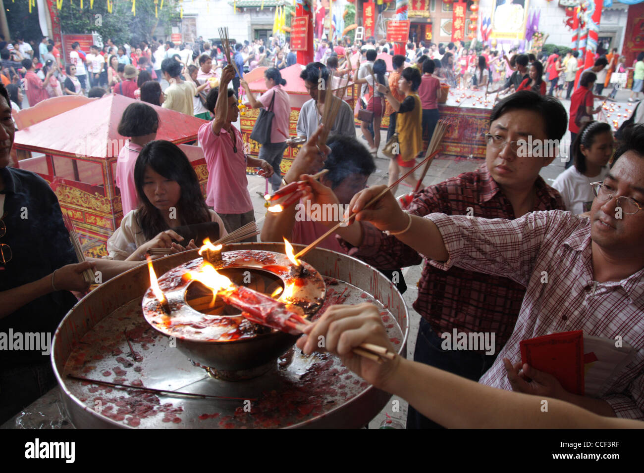 Thai people light incense sticks from lamp before offering prayers at a ...