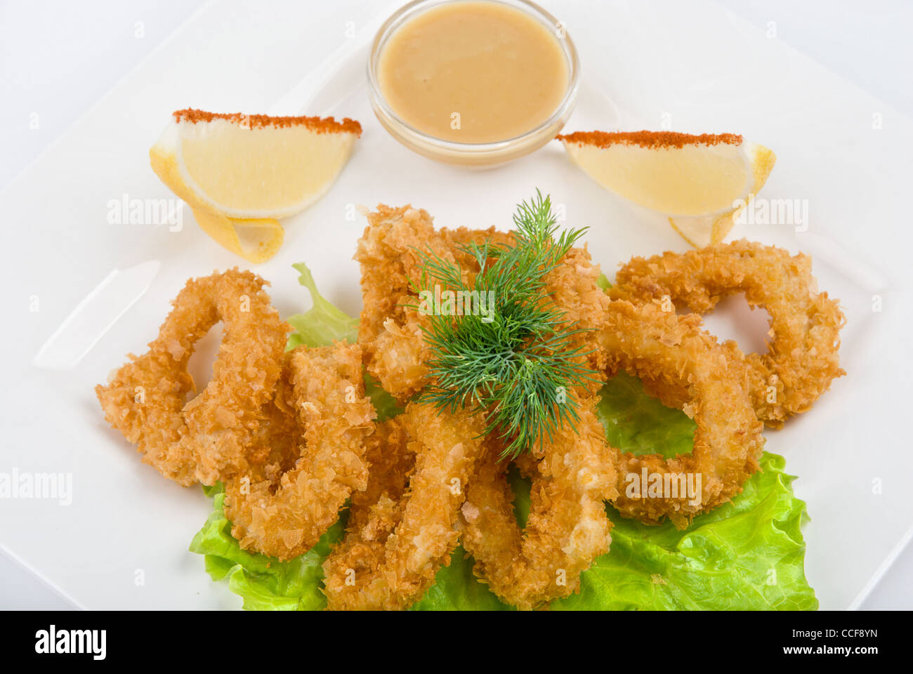 Deep-fried squid with salad leaves, sauce, green and lemon on a white ...