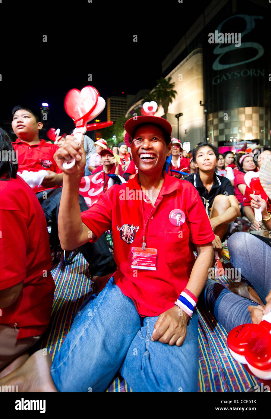 A Red Shirt smiles and shakes a clapper as her leader speaks on stage ...