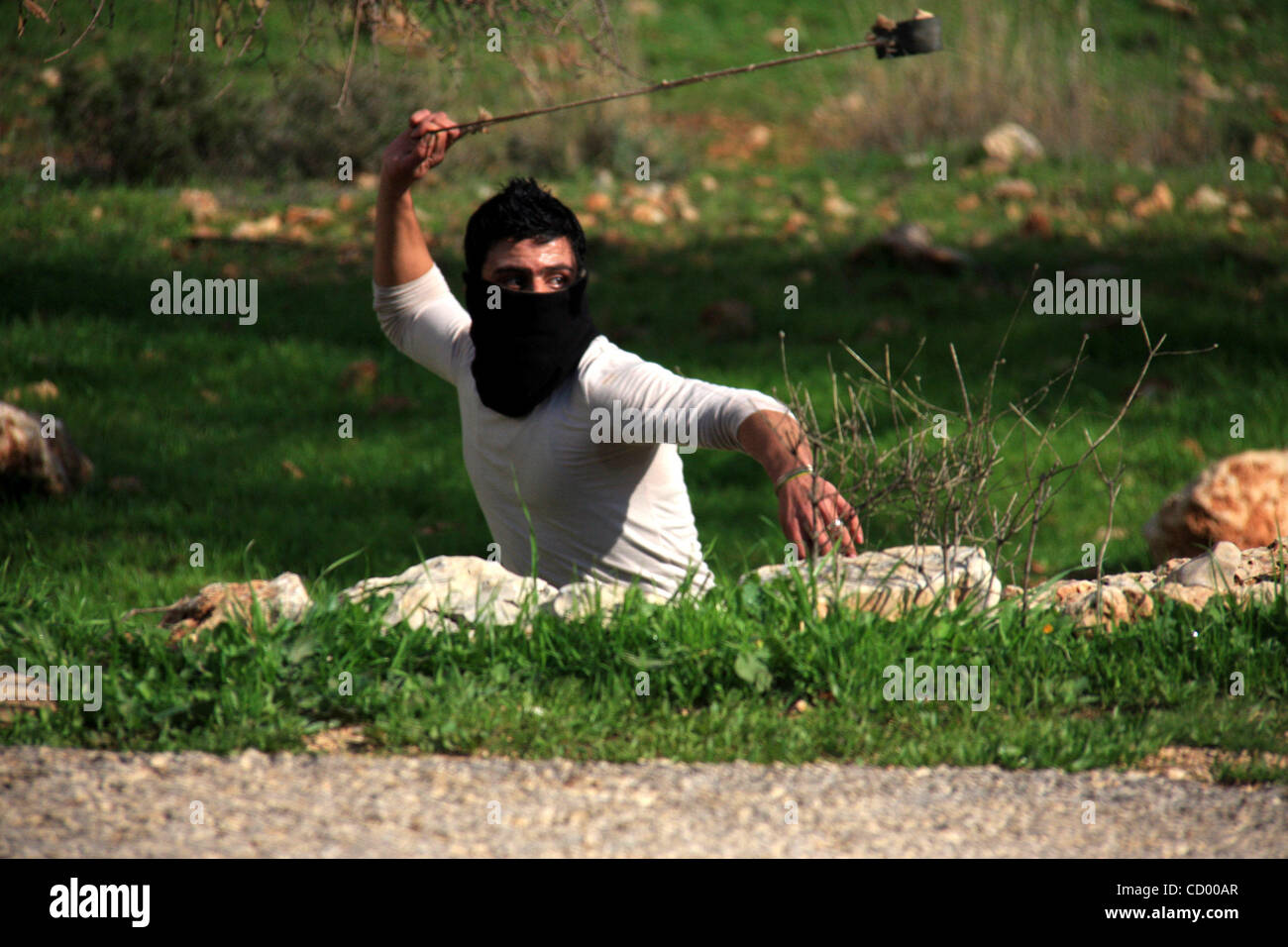 A Palestinian youth uses a sling to hurl stones towards Israeli ...