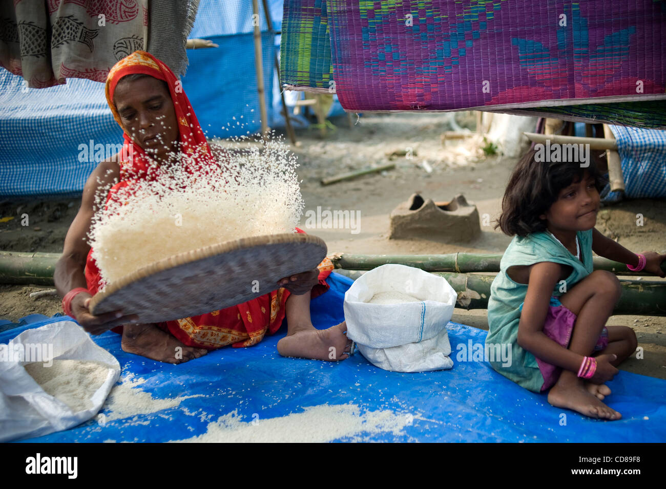 Wokilan Bibi, 45, winnows rice at her temporary shelter in Jhumka ...