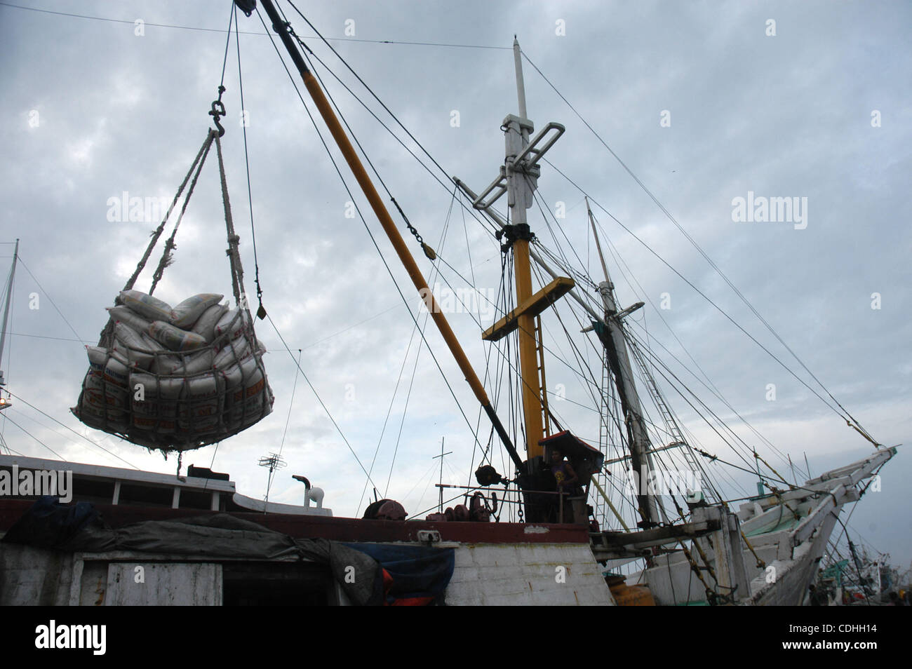 Workers load sacks of rice onto a traditional cargo ship for domestic ...