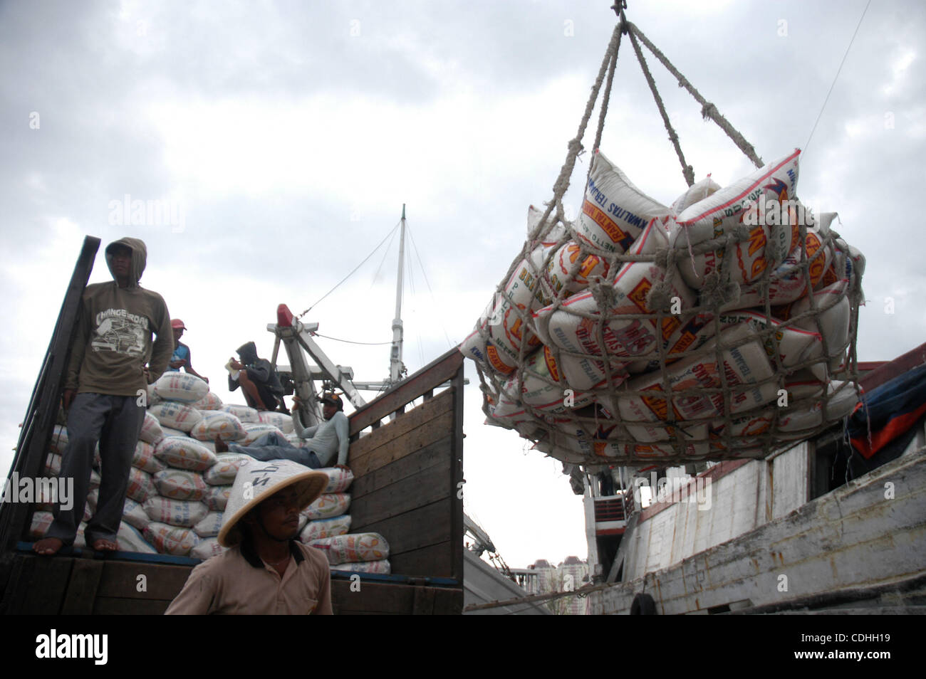 Workers load sacks of rice onto a traditional cargo ship for domestic ...
