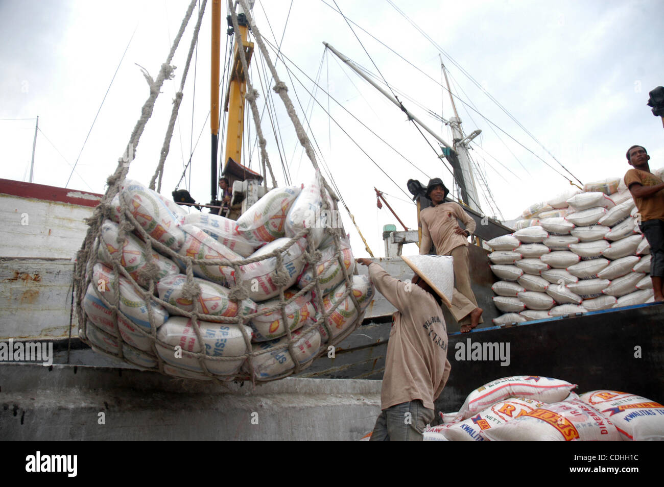 Workers load sacks of rice onto a traditional cargo ship for domestic ...