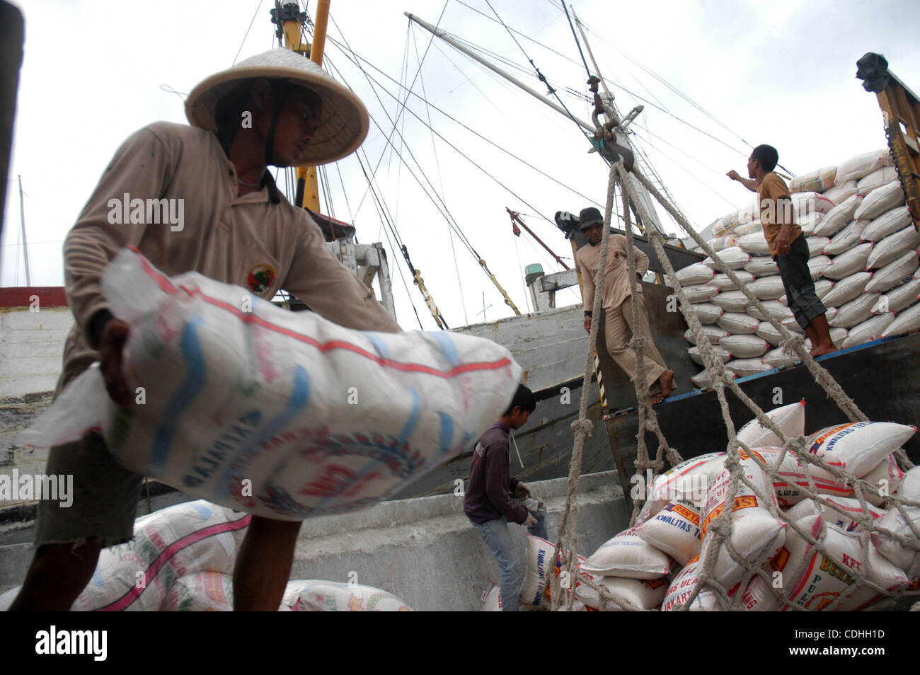 Workers load sacks of rice onto a traditional cargo ship for domestic ...