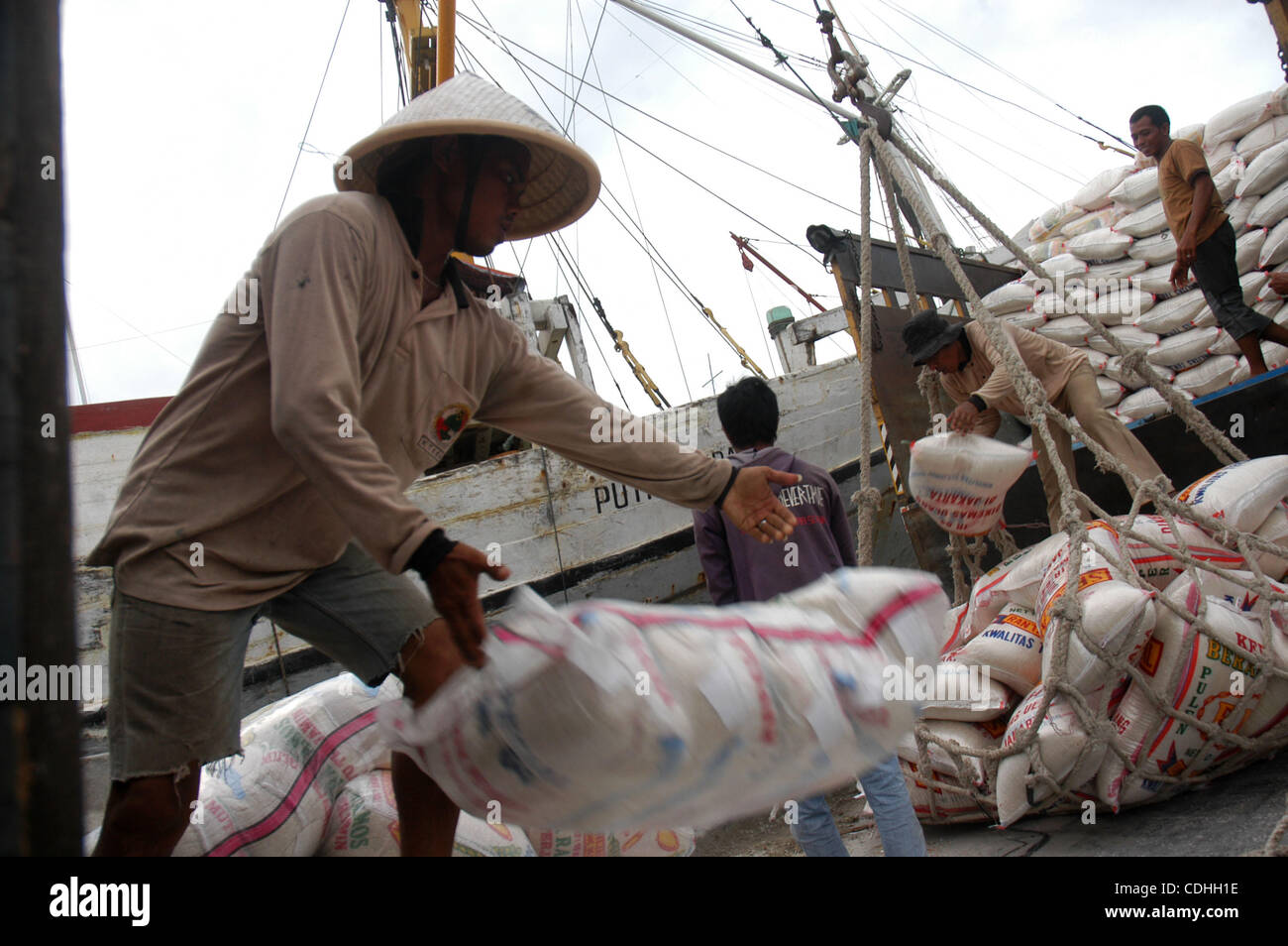 Workers load sacks of rice onto a traditional cargo ship for domestic ...