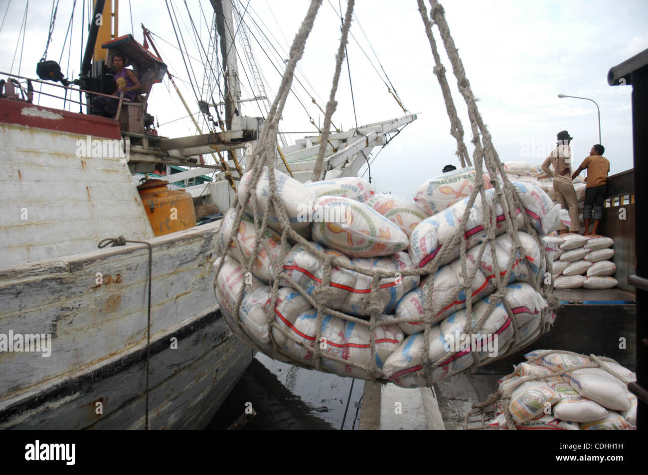 Workers load sacks of rice onto a traditional cargo ship for domestic ...